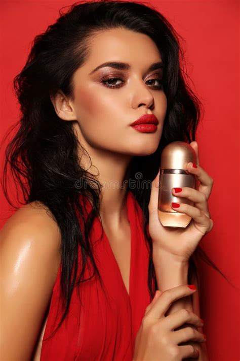 Woman With Dark Hair Wears Elegant Red Dress Holding Perfume In Hands