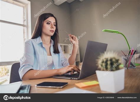 照片上，一个心事重重、可爱的女孩坐在办公桌前，上网本，眼镜嘴上戴着衬衫，坐在家里的办公室里 — 图库照片©deagreez1＃426039846