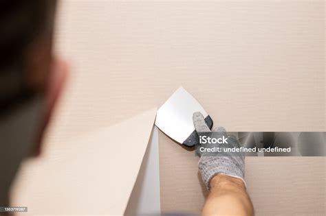 남자의 손 벽에서 오래된 빛 벽지를 찢어 홈 수리 작업에 대한 준비주걱으로 배경 화면을 제거 벽 방 수리를 업데이트하는 과정