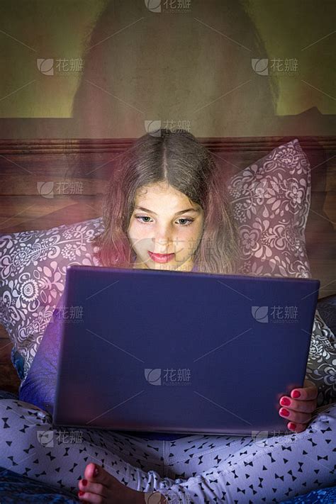 女孩坐在床上看着笔记本电脑脸上闪着红光