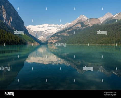 Crystal Clear Turquoise Waters Of Lake Louise Reflecting The Surrounding Forest And Snow Capped