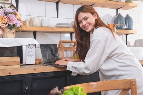 흰 셔츠에 아름다운 얼굴을 가진 여자는 부엌에서 빵 야채 과일 우유로 건강한 아침 식사를 만들고 요리 수업을 위해 노트북을 열고 있습니다 건강한 요리 아이디어 가정 생활에