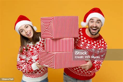 흥분 젊은 산타 커플 친구 남자 여자 빨간 스웨터 크리스마스 모자 노란색 배경 스튜디오 초상화에 고립 된 선물 상자와 함께 선물 상자를 개최 새해 축하 메리 홀리데이 컨셉