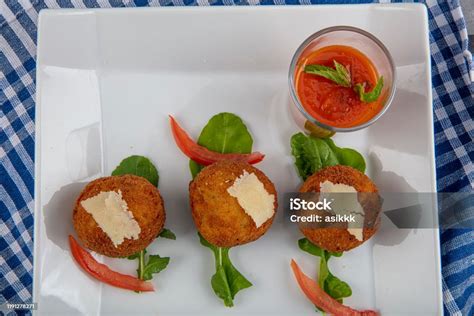 아란치니 맛있는 뜨거운 이탈리아 아란치니 녹인 치즈에 파마산 치즈를 얹은 사프란 주먹밥과 직사각형 접시에 아루굴라를 얹고 위에서