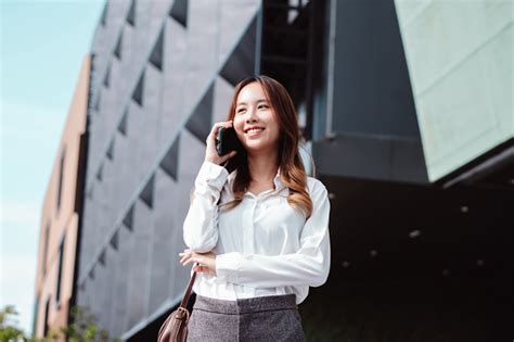 아름다운 아시아 여성 사업가는 스마트 폰을 사용하고 산책은 사무실 건물 근처의 현대 도시에서 통근하면서 웃는 것을 즐깁니다 25