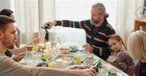 추수감사절에 가족 저녁 식사 중에 앞에 앉아 있는 엄마의 잔에 와인을 따르는 청년 사진 Unsplash의 테이블 이미지