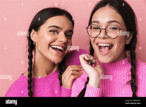 Two Cheerful Cute Teenage Girls Having Fun Isolated Over Pink Background Grimacing Looking At