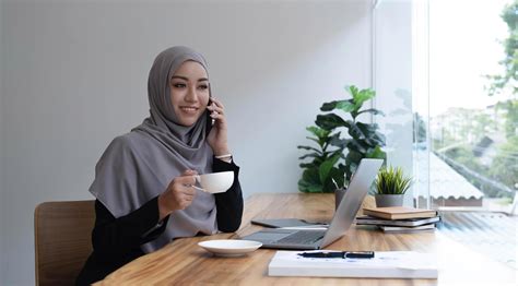 feliz y hermosa trabajadora musulmana sosteniendo una taza de café caliente sentada en la