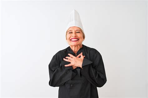 유니폼과 모자를 쓰고 고립된 흰색 배경 위에 서있는 중년 요리사 여성은 닫힌 눈과 얼굴에 감사하는 제스처로 가슴에 손을 대고 미소짓고 있습니다 건강 개념 명랑한에 대한 스톡