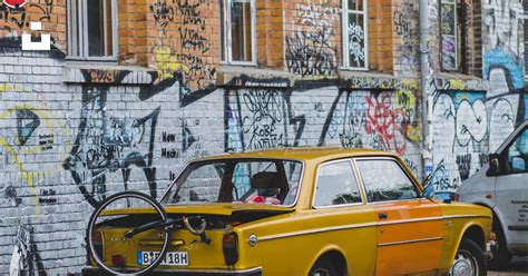 낙서 벽 근처의 뒤쪽 공원에 외발 자전거가 있는 빈티지 노란색 쿠페 사진 Unsplash의 무료 베를린 이미지