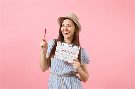 파란 드레스 모자 들고 빨간 연필 분홍색 배경에 고립 된 생리 일을 확인 하기 위한 여성 기간 일정에 행복 한 여자의 초상화