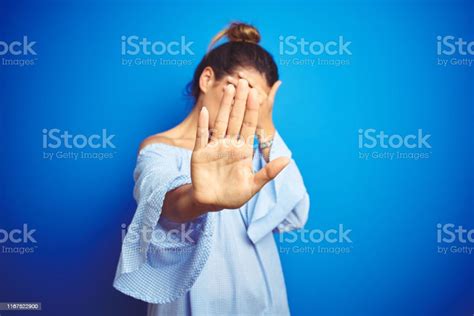 젊은 아름다운 여자는 손으로 눈을 덮고 슬프고 두려움 표정으로 중지 제스처를하고 파란색 고립 된 배경 위에 롤빵 헤어 스타일을