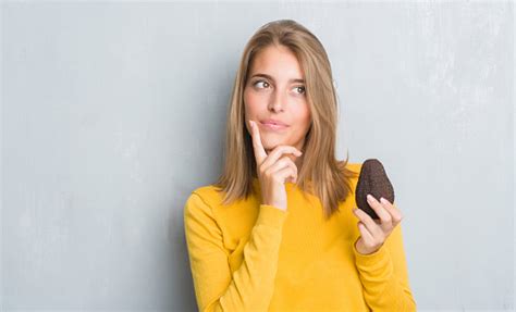 질문 매우 혼란 스 러 워 아이디어에 대 한 아름 다운 젊은 여 자가 그런 지 먹고 회색 벽에 아보카도 심각한 얼굴 생각 개념에