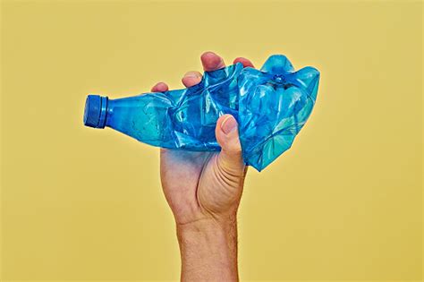 Tangan Meremas Botol Plastik Biru Dengan Latar Belakang Kuning Nol