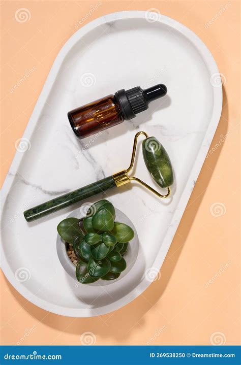 Hand Held Face Massager And Brown Glass Bottle With Dropper On Marble Plate Top View Stock