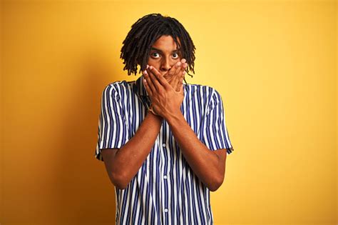 고립 된 노란색 배경 위에 캐주얼 스트라이프 티셔츠를 입고 공포를 가진 아프로 남자는 실수로 손으로 입을 덮는 충격을 받았다 비밀 개념입니다 가리기에 대한 스톡 사진 및