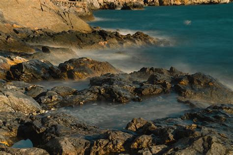 바다 너머로 해가 지면 바위가 흩어져 있는 해변에 파도가 부딪히며 황금빛 바다 풍경을 그리며 자연과 바다가 빚어낸 숨막히는 풍경을 드러냈습니다 0명에 대한 스톡 사진 및