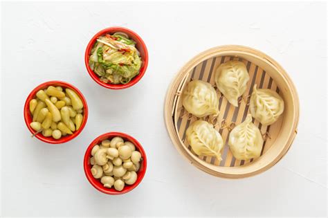 흰 테이블에 절인 버섯 양배추 고추를 곁들인 나무 이중 보일러에 다진 고기가 있는 삶은 만두 사만티 또는 원톤 수제 음식 위에서