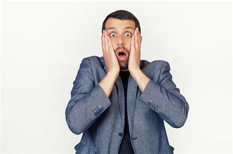 수염을 기고한 젊은 사업가 남자는 무서워하고 충격을 받았으며 그의 얼굴에 손을 대고 놀랐습니다 회색 배경에 남자의 초상화