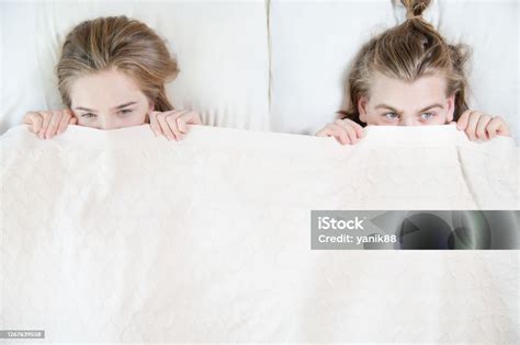 침대에 누워 있는 한 젊은 부부는 담요를 숨기고 담요 뒤에 숨어 있는 담요로 얼굴의 절반을 덮습니다 가족없는 문제와 대화의 부족의 개념 가리기에 대한 스톡 사진 및 기타