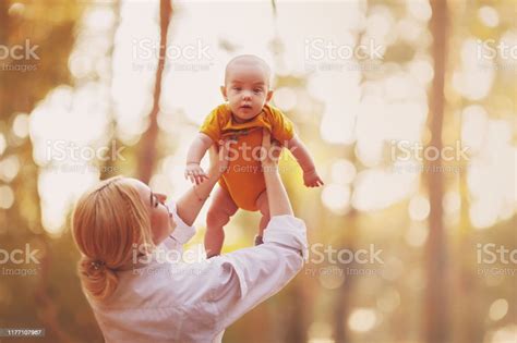 행복한 젊은 어머니는 아들과 함께 시간을 보내고 공기 속에서 높은 아기를 들어 올리고 있습니다 가을 숲 풍경에서 어린 아이와