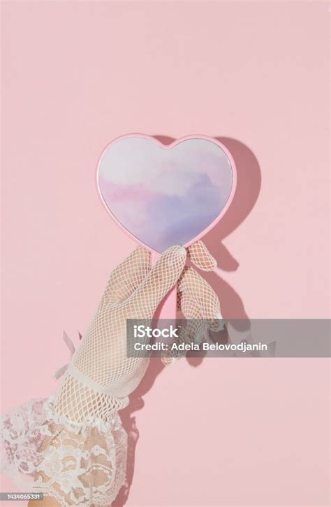 파스텔 아기 배경에 분홍색 구름이 반사 된 하트 모양의 거울을 들고있는 여성 손으로 발렌타인 데이 창조적 인 레이아웃 80 년대
