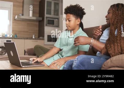 Mother Lovingly Assists Her Son In Using Laptop In Living Room At Home Guiding Him With Patience