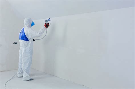 공기없는 스프레이 페인트 작업자는 흰색으로 공기가 없는 스프레이로 벽을 페인트하고 숙련된 작업자가 기계식 공기 도구로 표면에