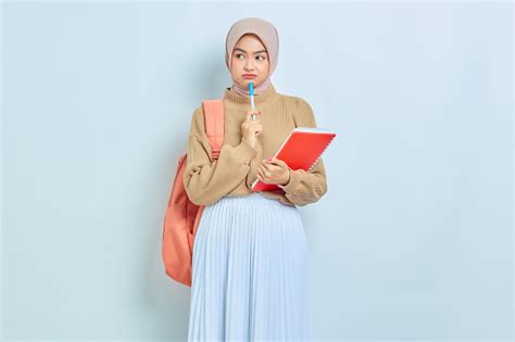 갈색 스웨터와 배낭을 입은 젊은 아시아 무슬림 여성 학생은 책과 펜을 들고 흰색 배경에 고립 된 것을 생각합니다 학교 개념으로