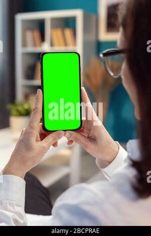 Chroma key compositing. Woman holding smartphone with green screen indoors, closeup. Mockup for ...