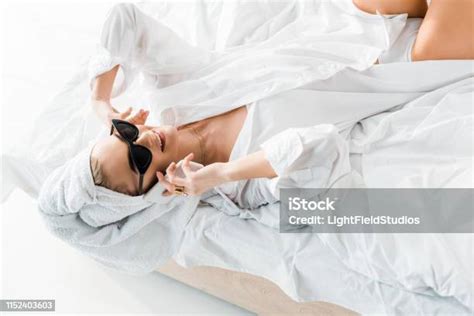 젊은 웃는 여자 셔츠 선글라스 보석 및 침대에서 스마트 폰에 얘기 하는 머리에 수건으로 개인 장식품에 대한 스톡 사진 및 기타 이미지 개인 장식품 누워있기 명랑한