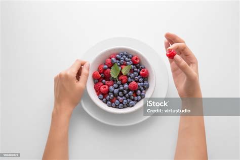 그릇에 신선한 장과 을 먹는 젊은 여자 위에서 직접 볼 수 있습니다 흰색 접시에서의 여성 손 따기 건강 한 열매 상위 뷰 건강한