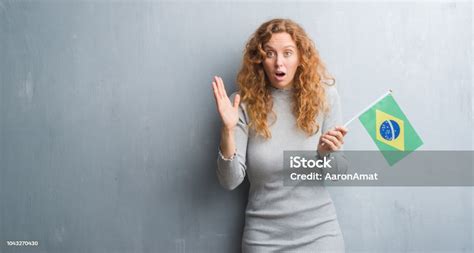 그런 지 회색 벽 지주에 젊은 빨강 머리 여자 브라질 매우 행복 하 고 흥분 상자 식 축 하 승리 큰 웃음과 비명과 손을의 깃발