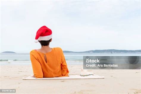 빨간 크리스마스 모자를 쓰고 수건에 흰 밀짚모자를 쓴 채 해변에 앉아 있는 여자 40 44세에 대한 스톡 사진 및 기타 이미지 40 44세 갈리시아 공휴일 Istock