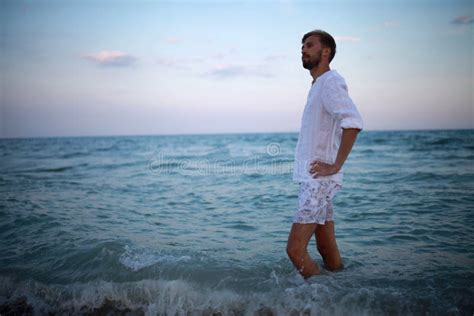 Young Pensive Man Stands In Water On Beach In Evening Stock Image