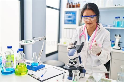 Young Chinese Woman Wearing Scientist Uniform Using Microscope At
