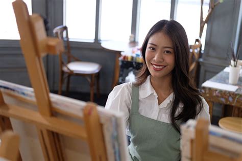 여자는 스튜디오에서 유성 물감으로 캔버스에 그림을 그린다 여성 예술가가 작업장에서 그림을 그린다 젊은 여성 예술가는 붓으로