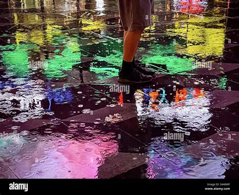 Low Section Of Mans Legs And Feet Standing On Wet Reflective Paving