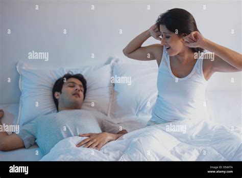 Man Snoring With His Wife Covering Ears With Fingers On The Bed Stock
