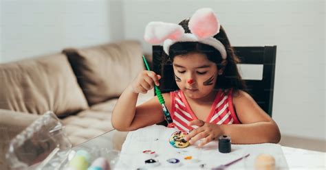 イースター、おめでとう！イースターエッグを描く美しい子供の女の子。イースターの準備をしている幸せな家族。イースターの日にバニーの耳を身に着けて