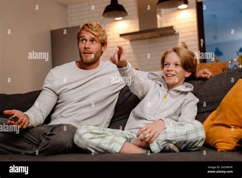 Ginger Father And Son Smiling And Watching Tv While Resting On Couch At
