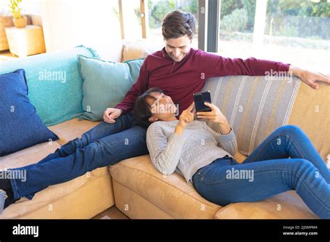 Smiling Asian Girlfriend Using Smartphone While Lying On Caucasian
