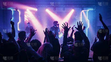一支由吉他手和鼓手组成的摇滚乐队在夜总会的音乐会上表演。前排人群在狂欢。舞台上明亮的彩色频闪灯前，歌