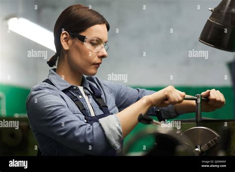 Focused Middle Aged Female Manual Lathe Operator Twisting Metal Handle While Preparing Machine