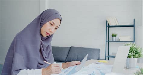 아름 다운 아시아 무슬림 아가씨는 집에서 거실에서 노트북을 사용 하 여 머리 스카프 캐주얼 웨어를 입고 있습니다 원격 재택