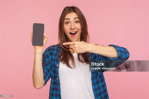 놀라운 응용 프로그램 모바일 장치 광고 놀란 소녀 에 격자 무늬 셔츠 가리키는 에 휴대 전화 화면 과 보고 충격 가리키기에 대한