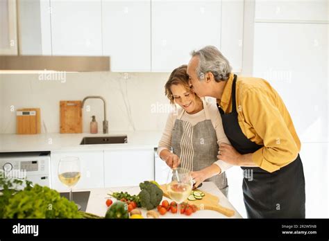 Loving Senior Husband Hugging And Kissing His Smiling Spouse At Cozy