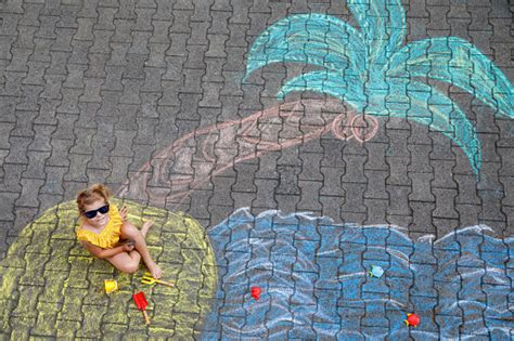 바다 모래 아스팔트에 화려한 분필로 칠해진 손바닥으로 수영복을 입은 행복한 어린 미취학 소녀 분필 그림으로 재미있게 지내는 귀여운 아이 여름 휴가 여름 공기 주입에 대한