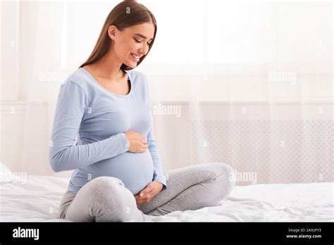 Expectant Girl Touching Belly Smiling Sitting On Bed In Bedroom Stock