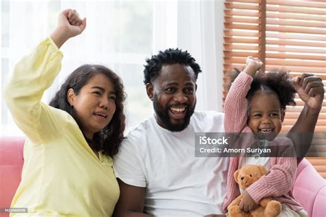 집에서 거실의 소파에 앉아있는 동안 함께 놀고 함께 포옹하고 Tv를 보면서 놀고있는 행복한 아프리카 계 미국인 가족 소파에서 시간을 보내는 웃는 부모와 십대 딸 2 3 살에